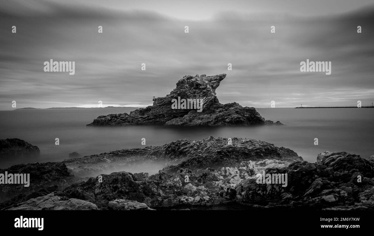 A grayscale view of a seascape with rocks and sky after sunset with ...