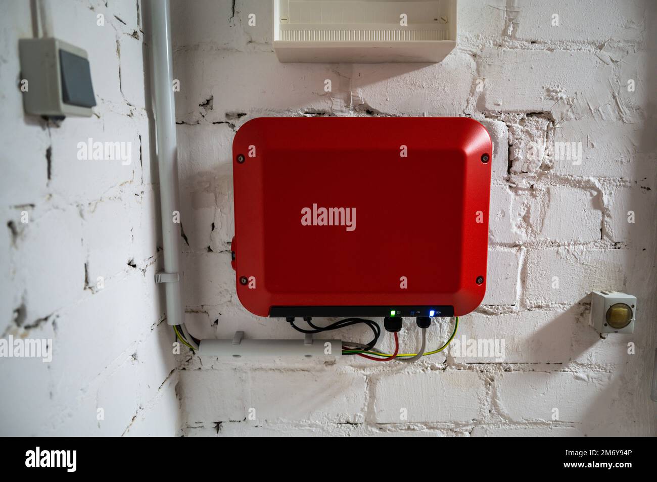Red inverter of a photovoltaic system mounted on a white basement wall ...