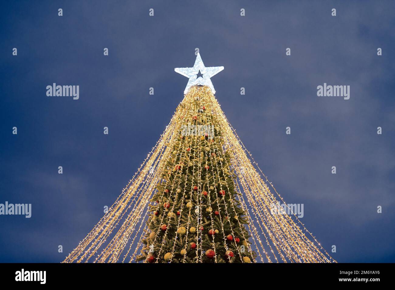 Christmas tree with yellow garlands, decorative bulbs and big white ...