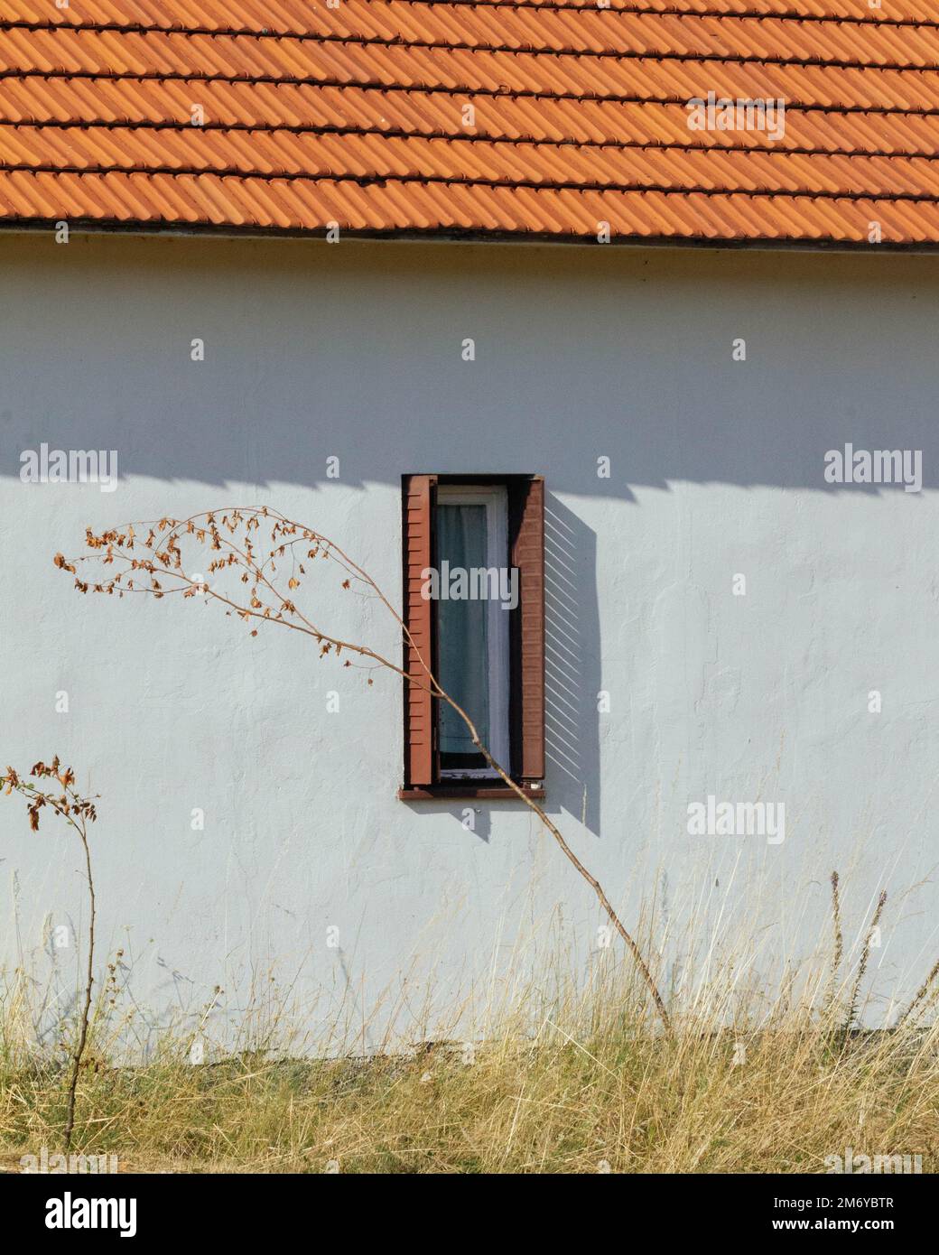 A vertical shot of the small window on the white wall of the house with ...