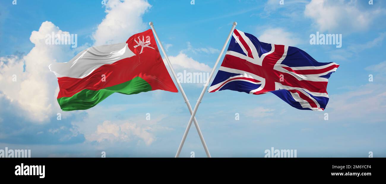 two crossed flags Great Britain and Oman waving in wind at cloudy sky ...