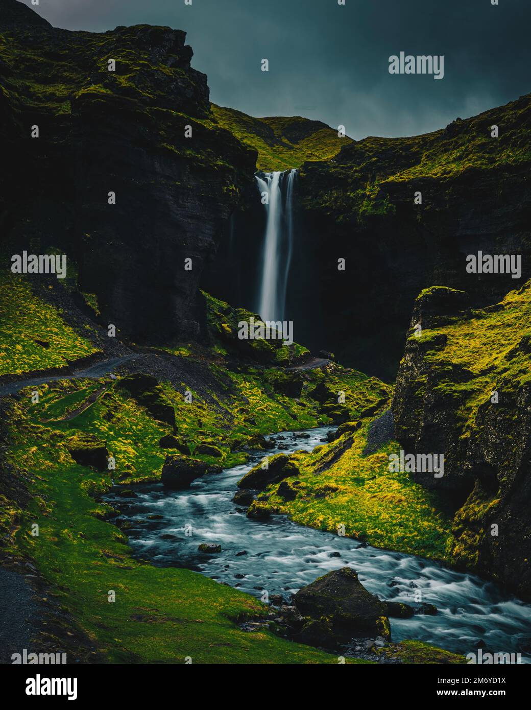 A vertical shot of a beautiful waterfall and a small stream in Iceland ...