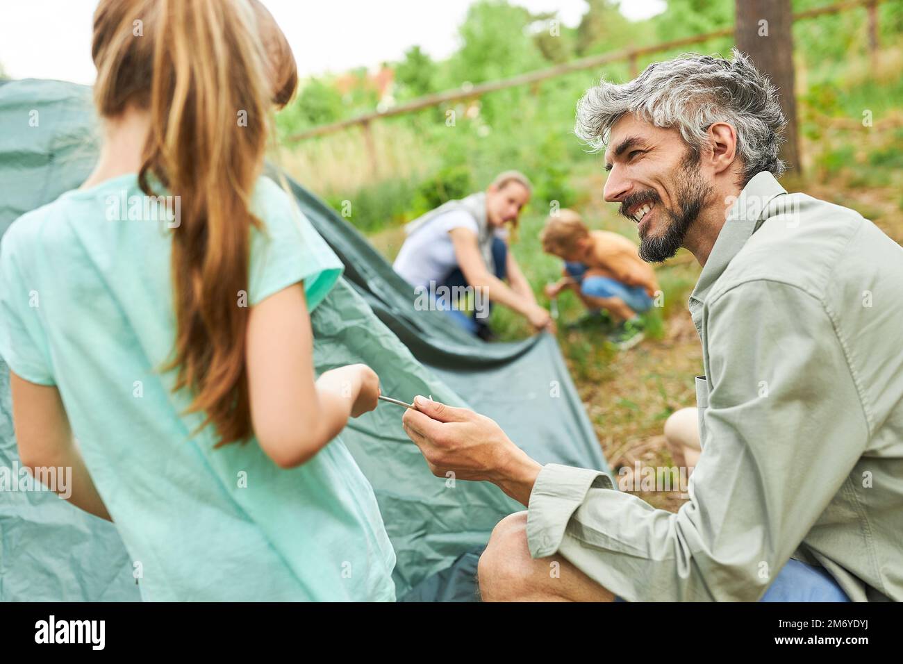 Daughter helping happy father in setting up tent while camping in ...