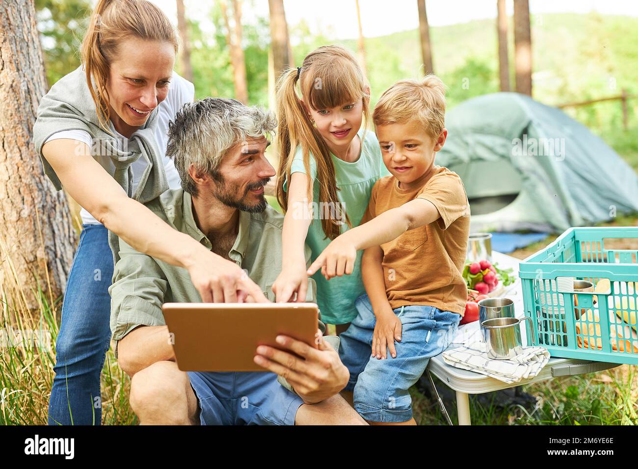 Family pointing at digital tablet held by man while camping in forest ...