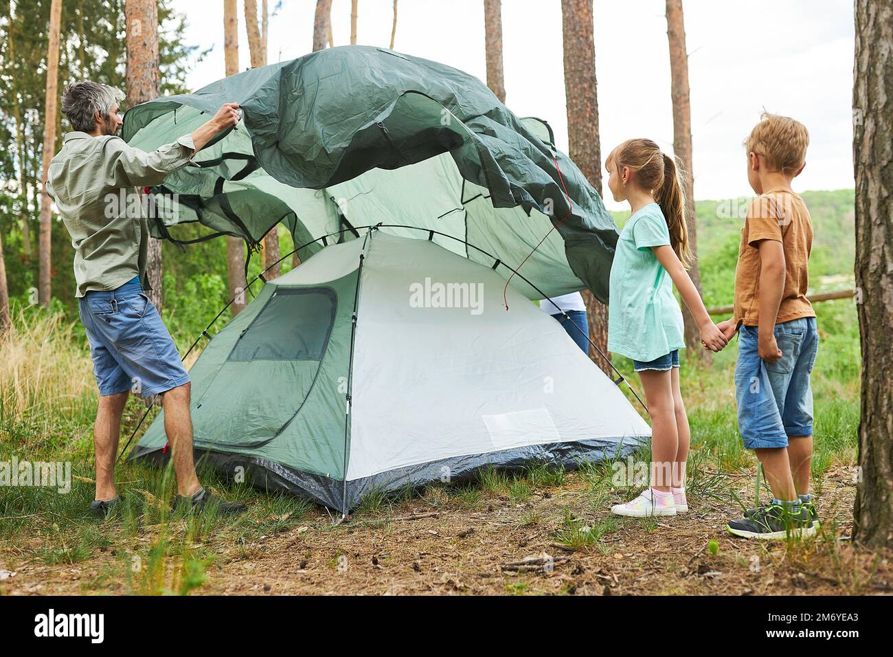Children looking at parents setting up tent while camping in forest ...