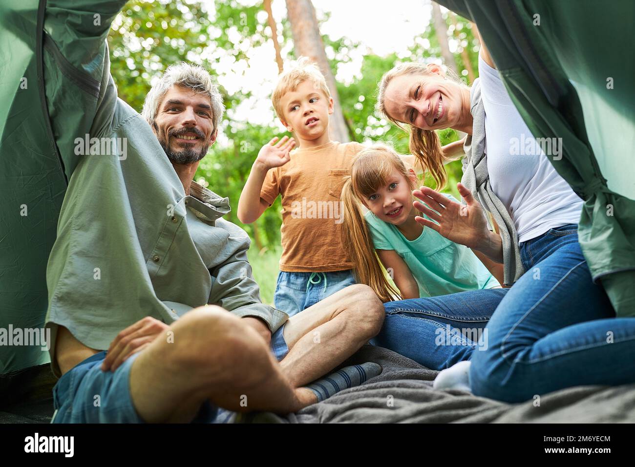 Happy parents waving hands while setting up tent with children in ...