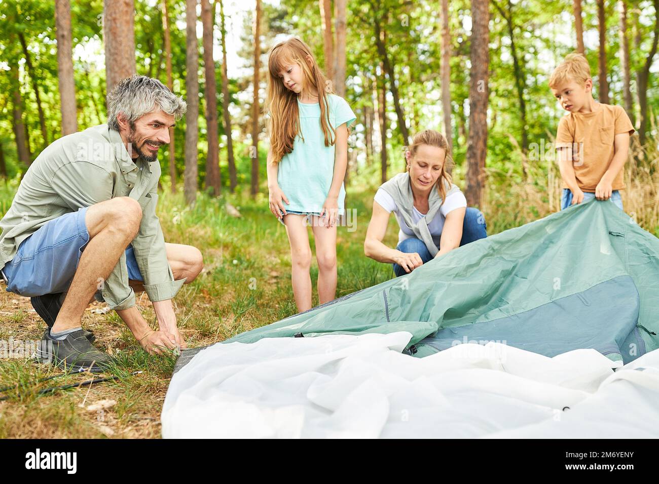 Parents setting up tent for camping with kids in forest during summer ...