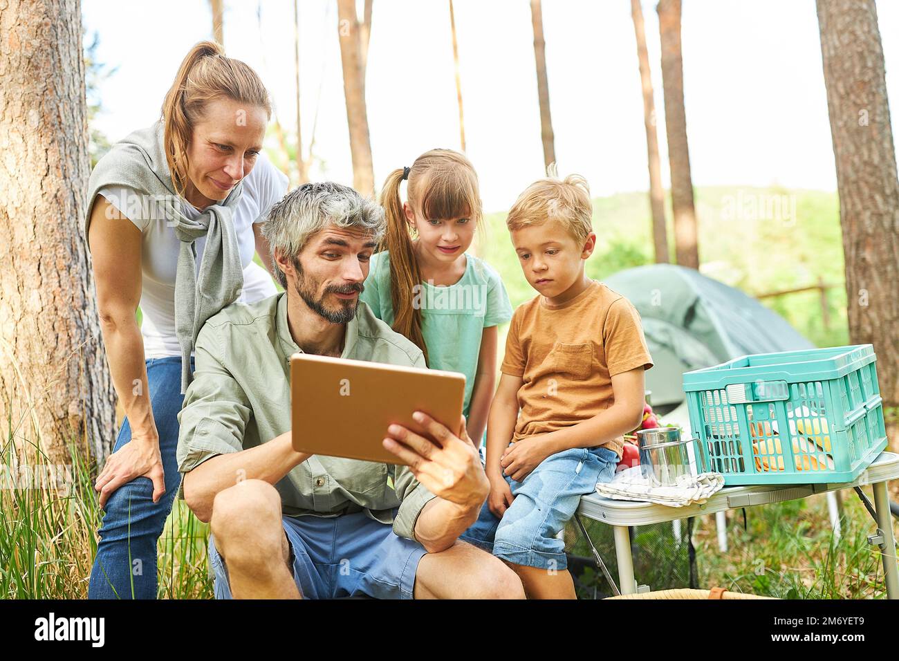 Man sharing digital tablet with family while camping in forest during ...