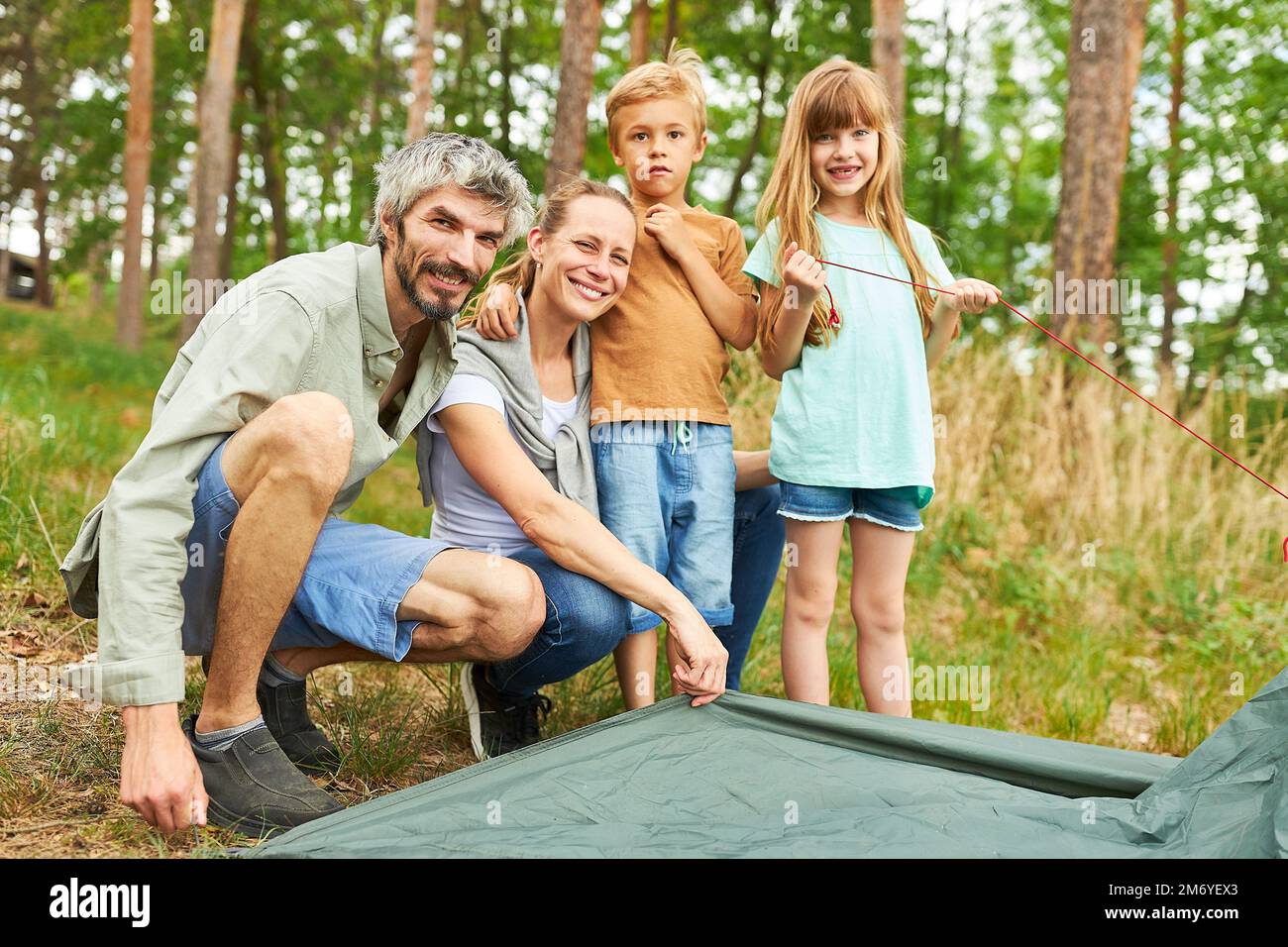 Portrait of happy parents with children setting up tent while camping ...