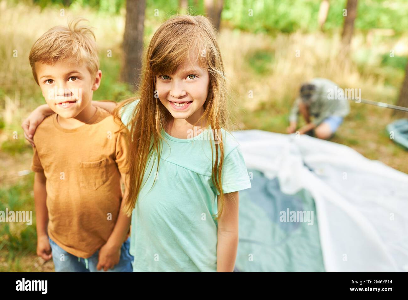 Portrait of smiling sister and brother standing in front of tent while ...