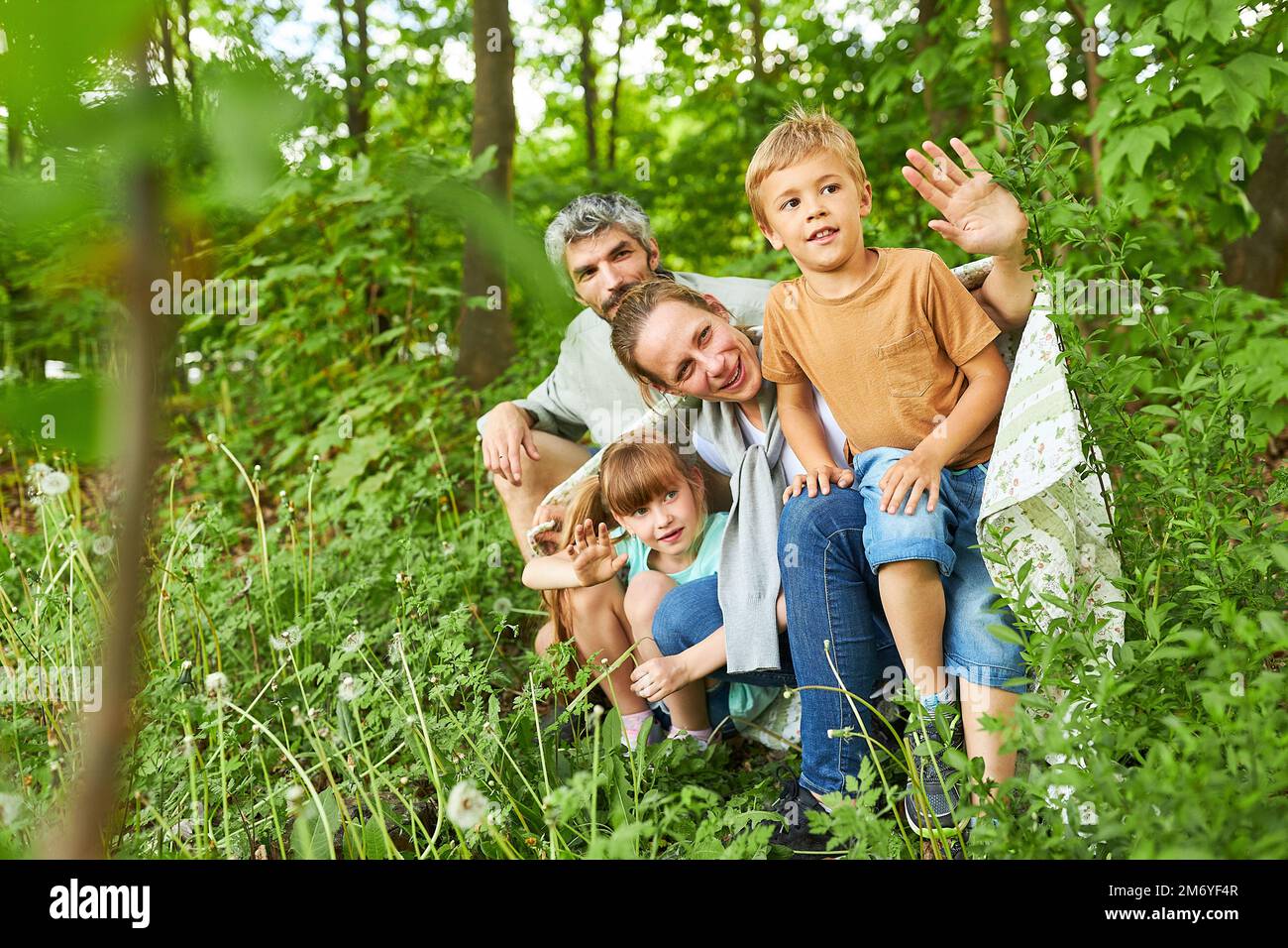 Happy woman waving while hiking with children and man in nature during ...