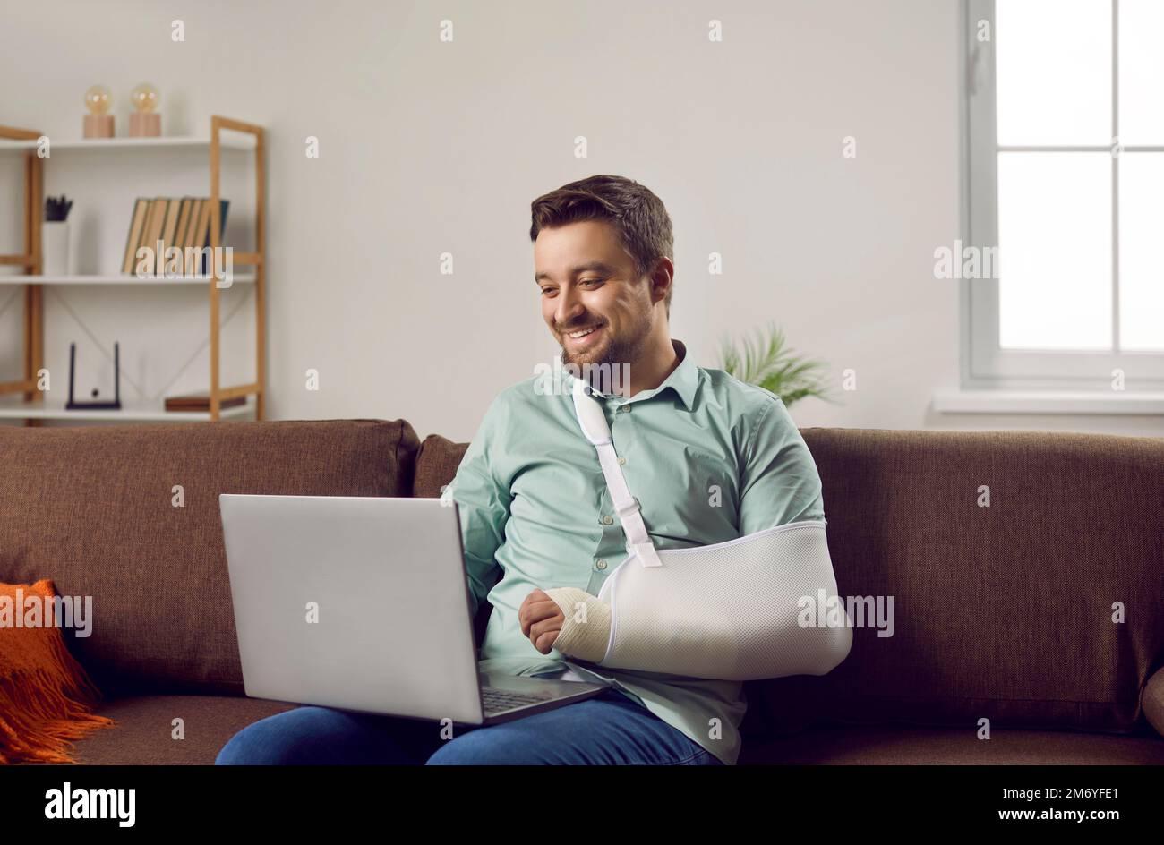 Happy young man with arm in a cast sitting on the couch at home and ...