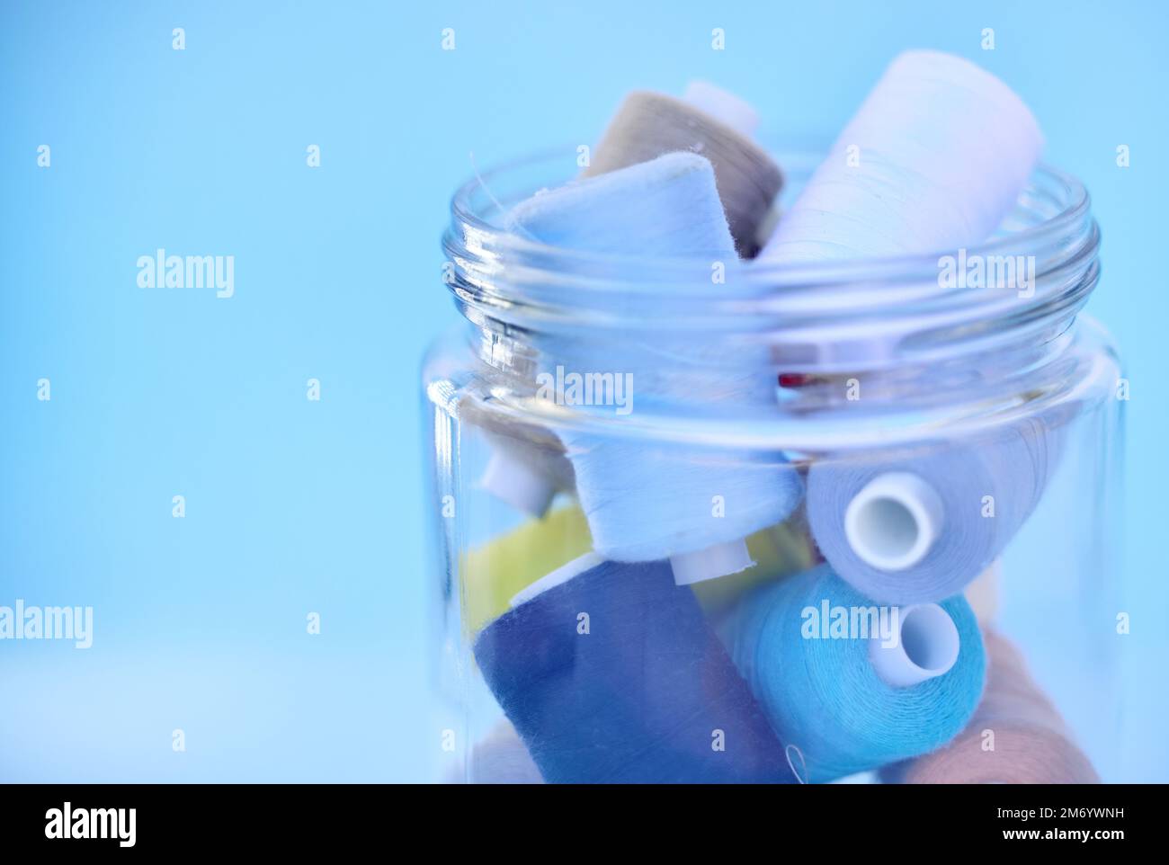 Sewing thread, glass jar and blue background for craft, tailor or ...