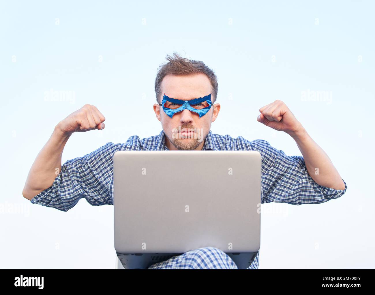 Adorable man in nightwear shirt and superhero blue mask using laptop ...
