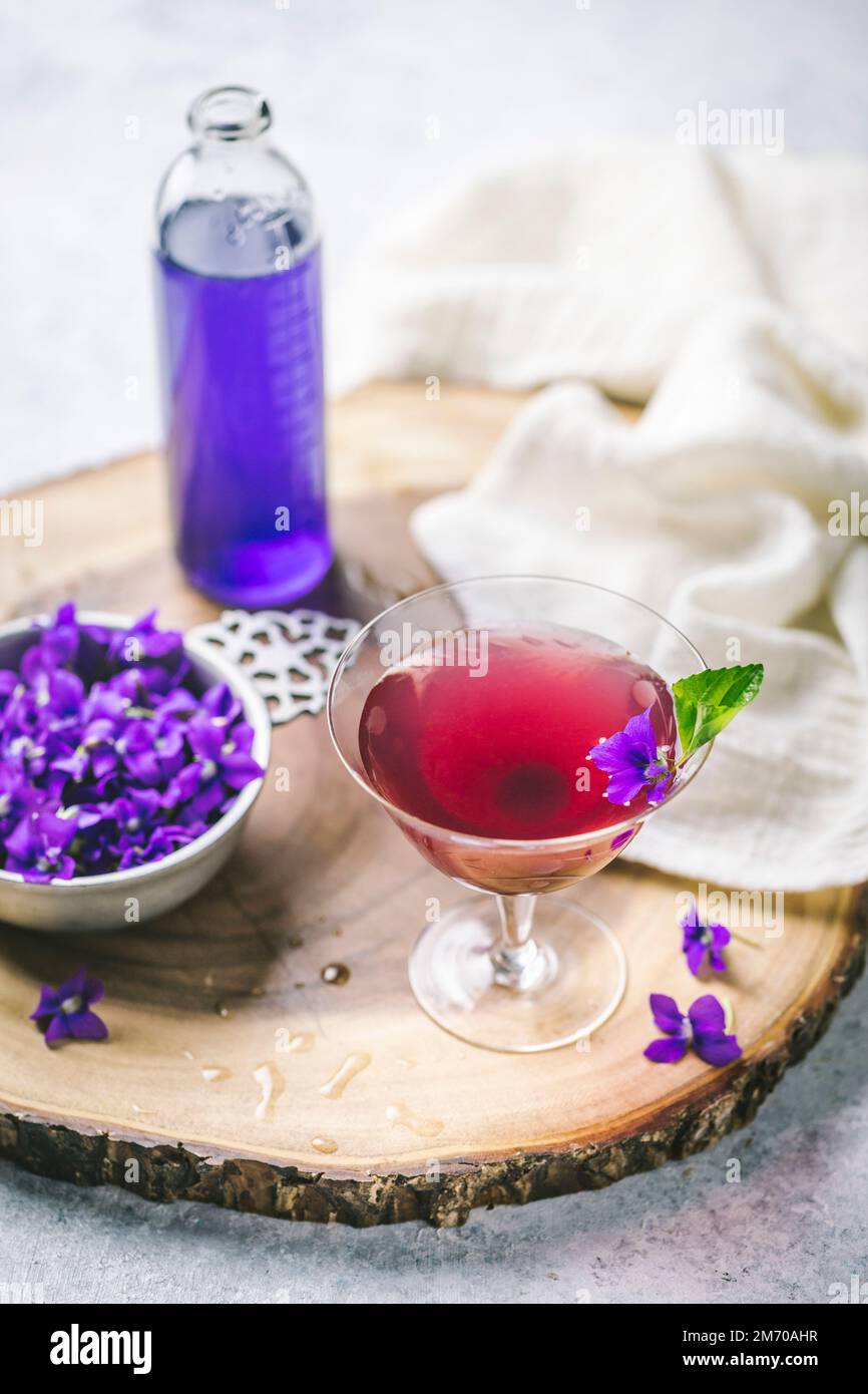 Pink cocktail in vintage glass with flower garnish, flowers and violet ...