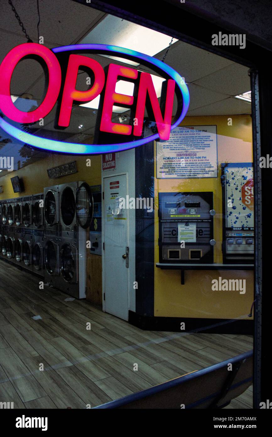 A vertical shot of an open sign hanging on a window of a laundromat ...