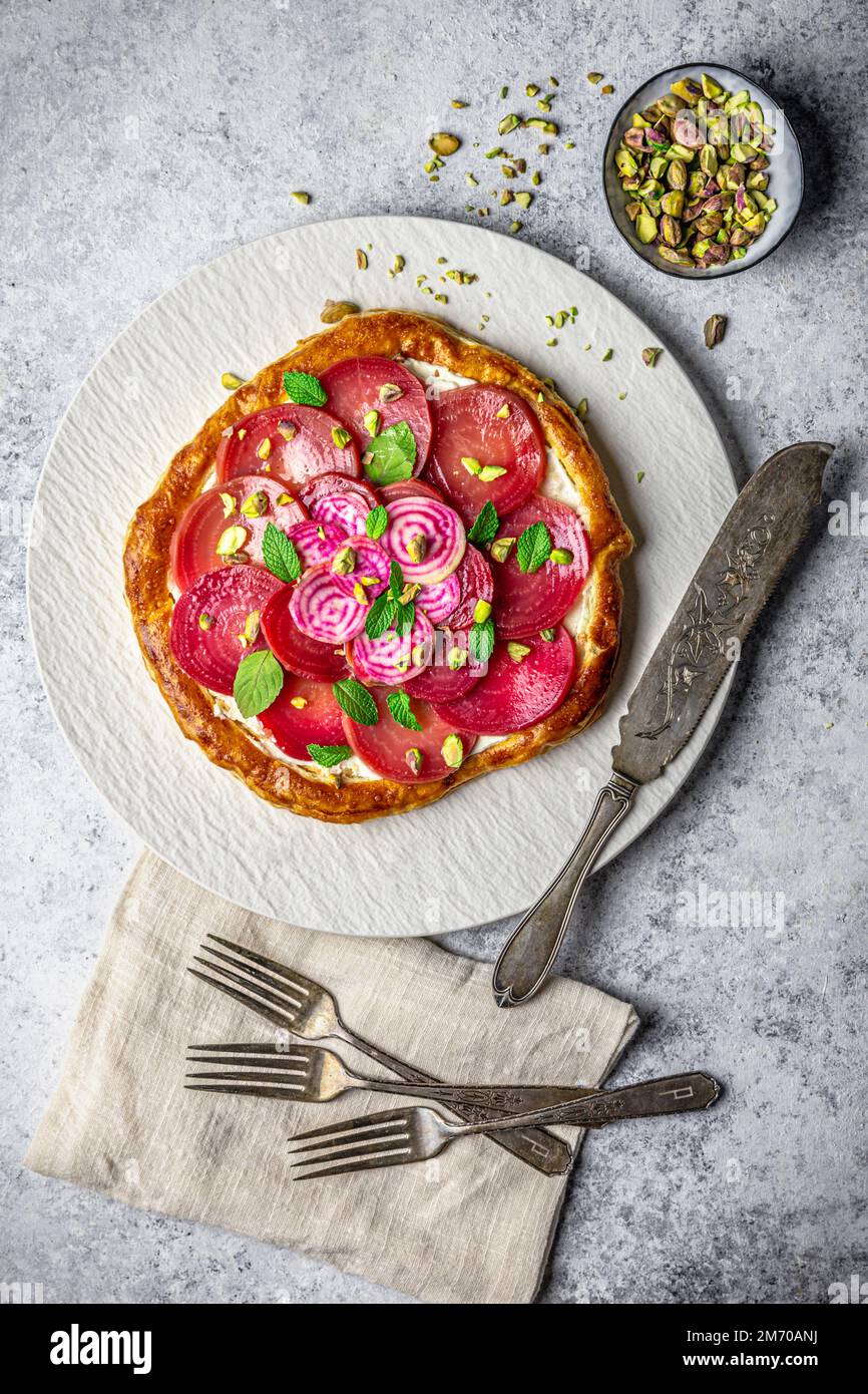 Round pastry tart with sliced beets, feta and mint leaves on white ...