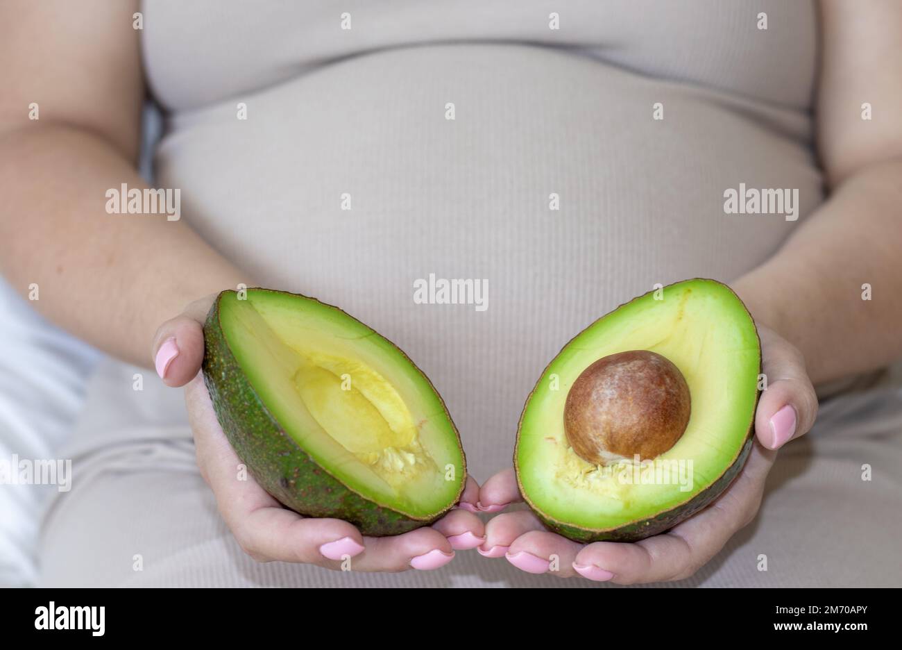 pregnant woman on bed advanced belly with avocado bun baby clothes in ...