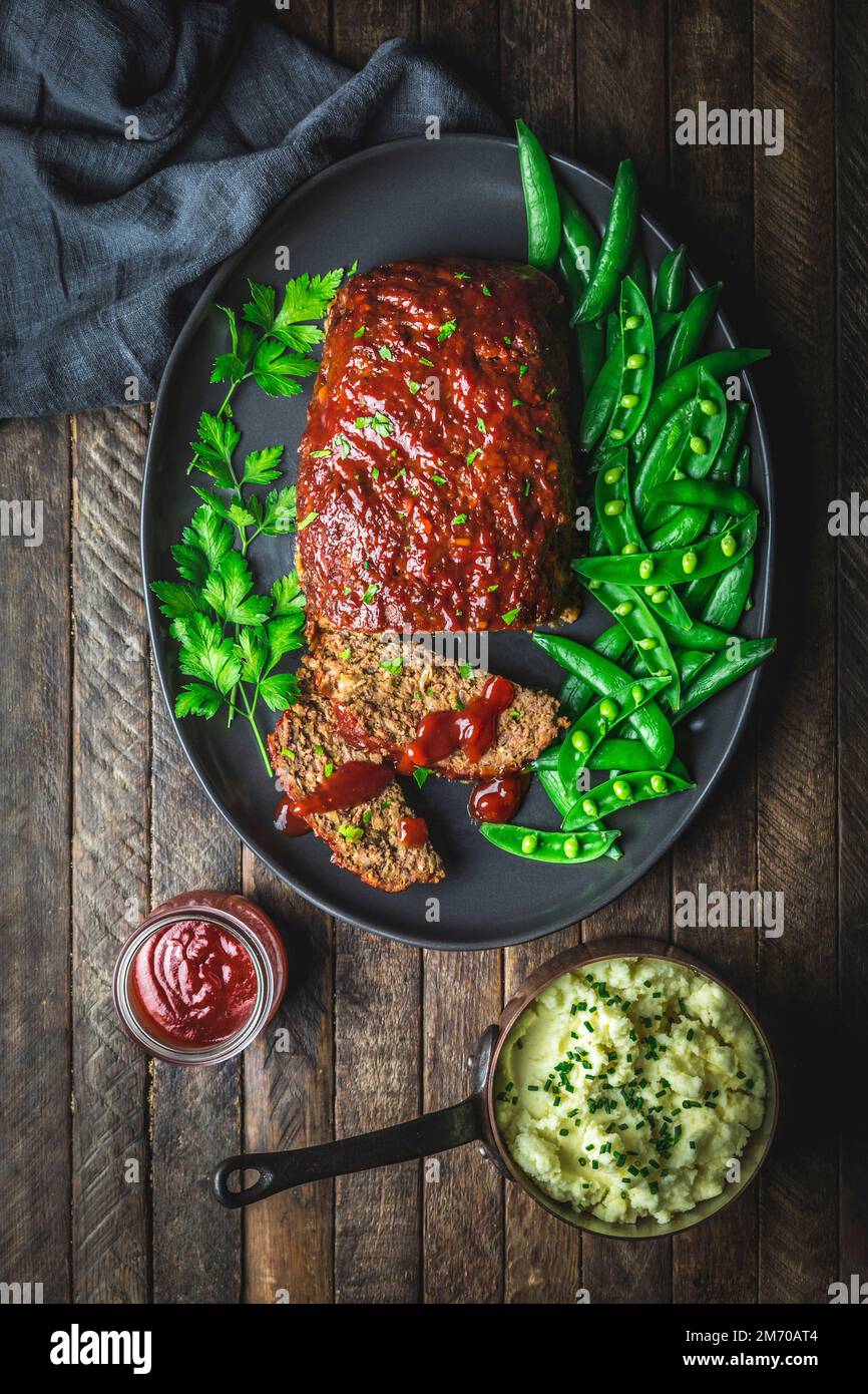 Meatloaf and slices on platter with fresh snap peas, mashed potato in ...