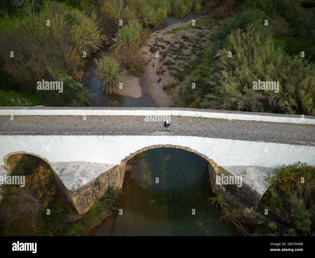 An aerial view of a person standing on a cobblestone arch bridge above ...