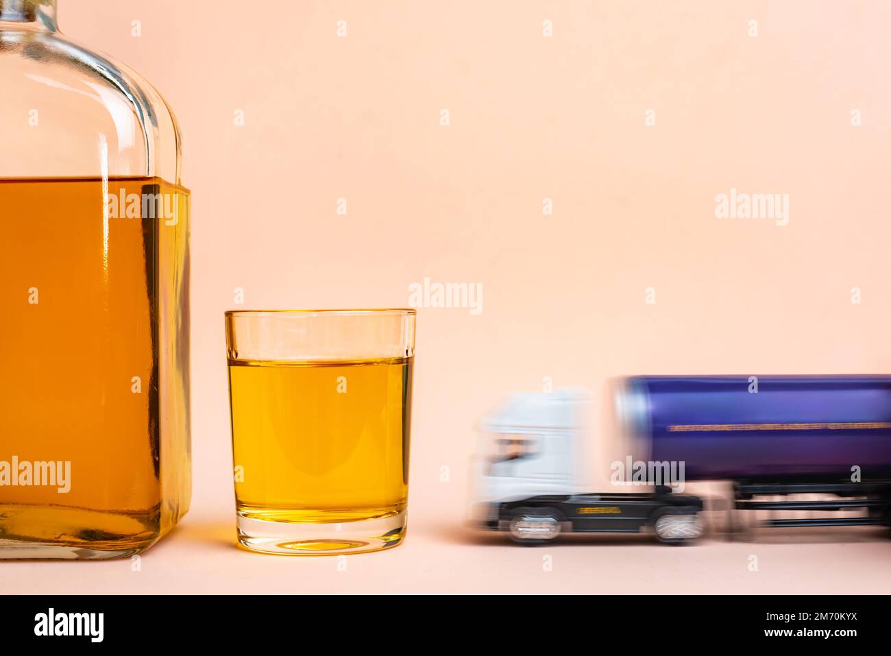 Bottle and shot glass with whiskey, a toy tanker truck at high speed is ...