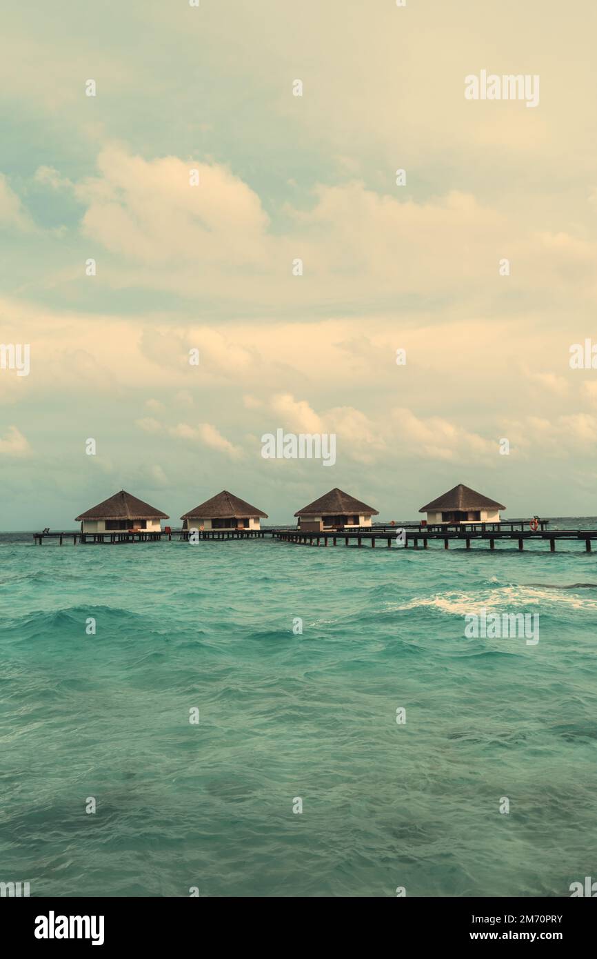 A vertical shot of a row of four typical overwater bungalows with triangle canopy roofs and a ...