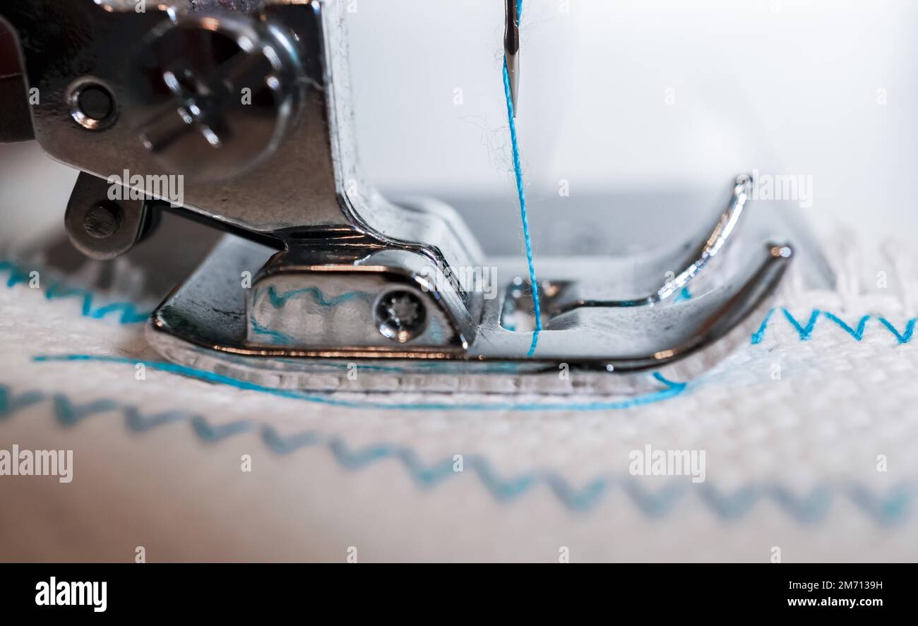Close-up of sewing machine needle with blue thread sewing on a white ...
