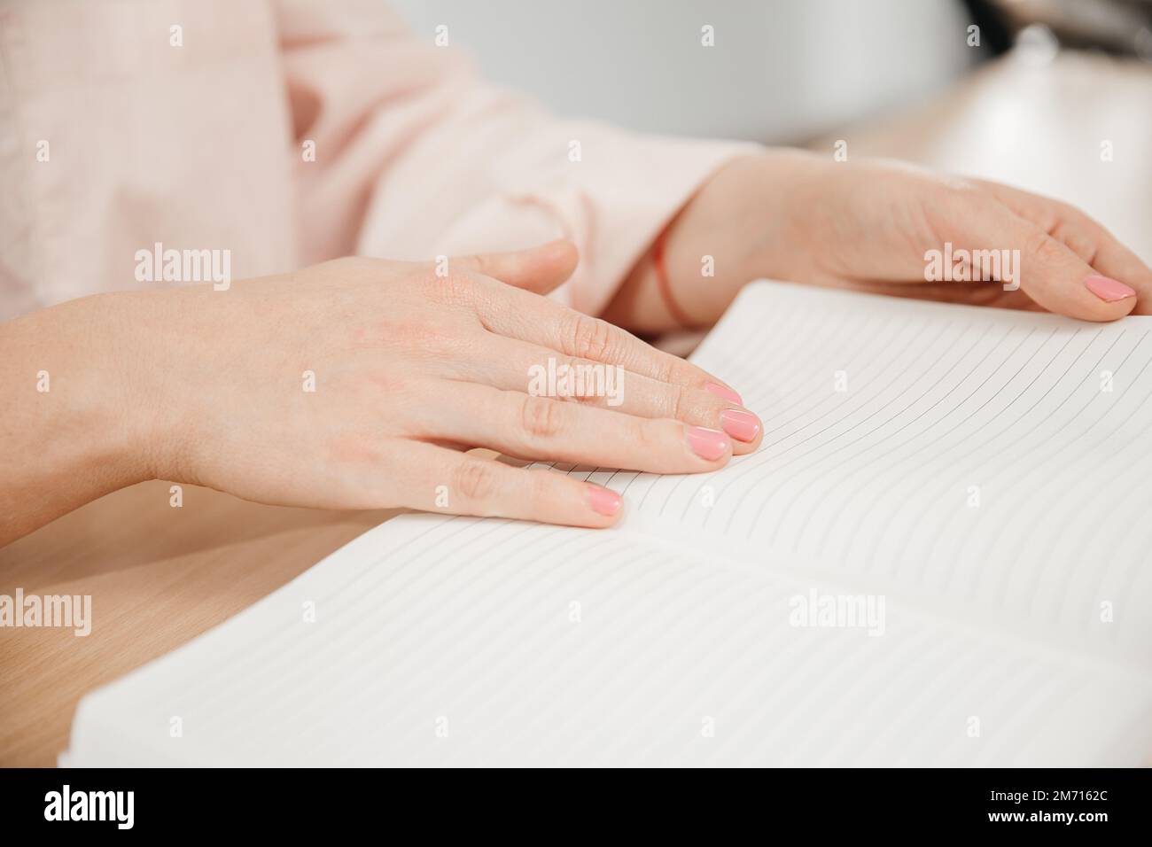 Close up of a woman's hands writing in a notebook placed on a wooden ...