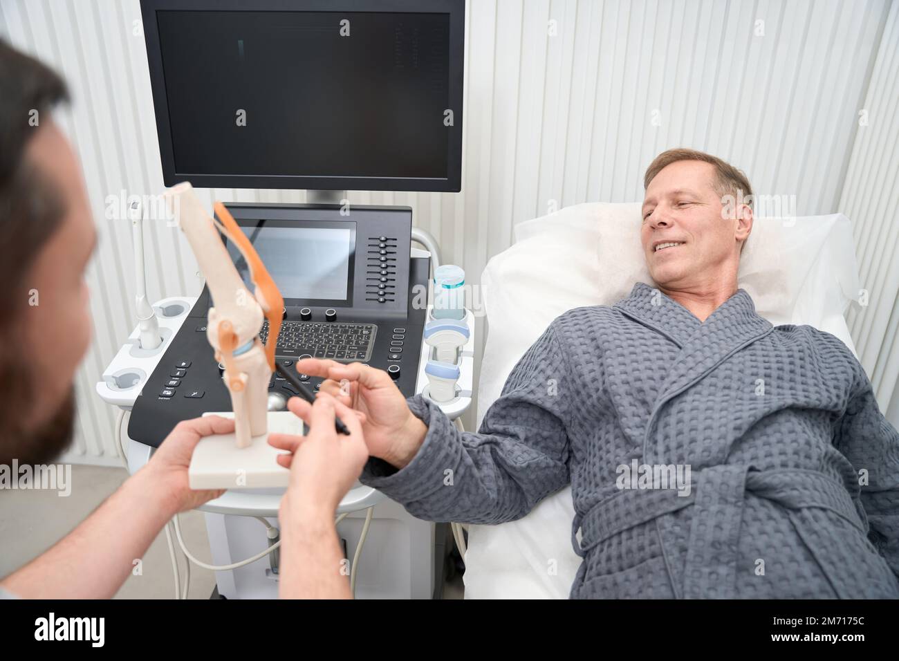Adult man in hospital gown inquiring about human knee anatomy Stock ...
