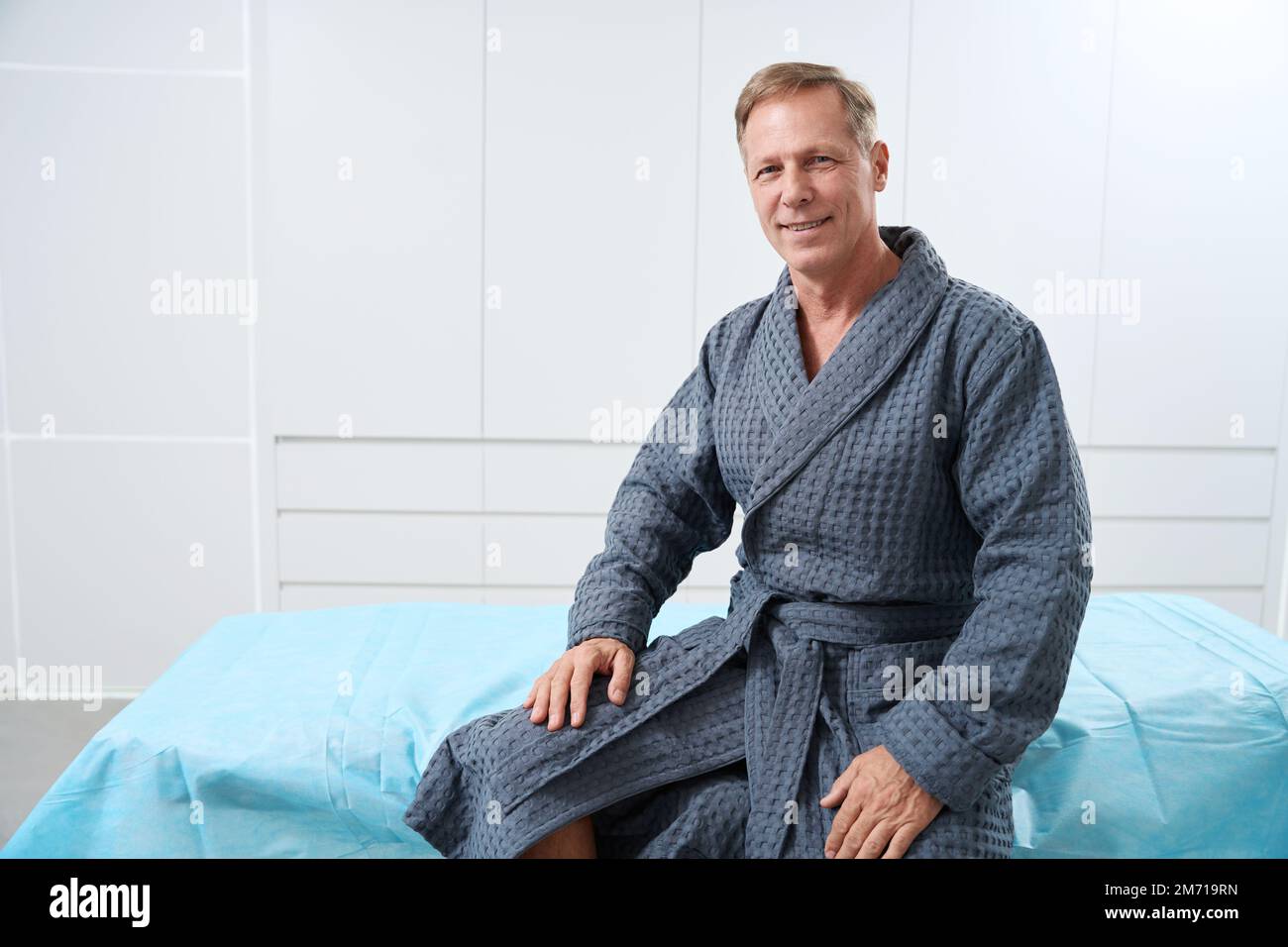 Smiling man in a hospital gown sits on a bed Stock Photo - Alamy