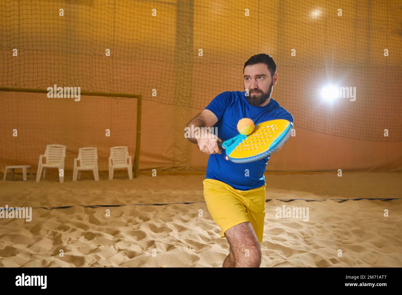 Man on sand court indoors making pass with tennis ball Stock Photo - Alamy