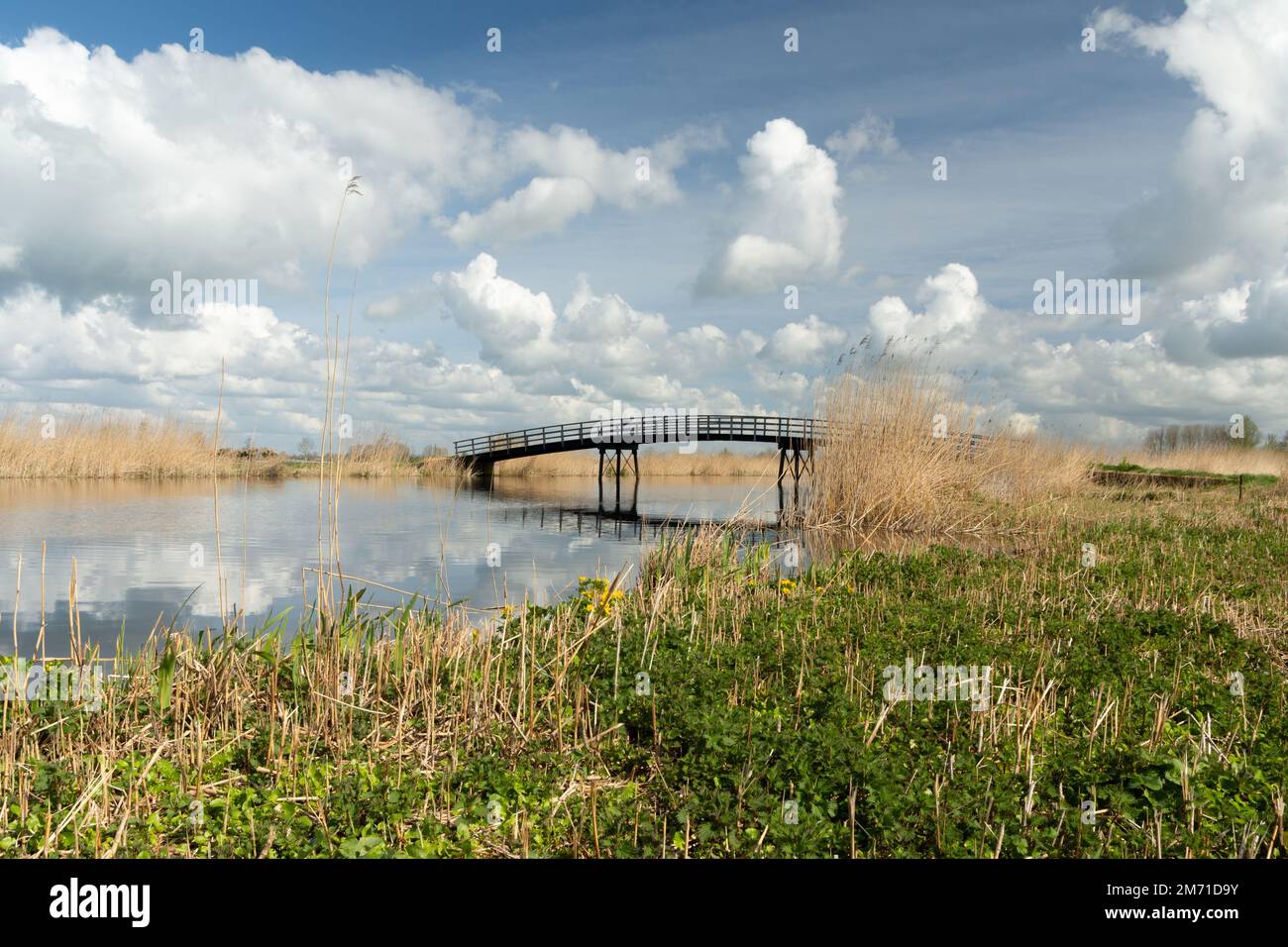 A barren field with dry grass and a bridge over a river, on a sunny day ...