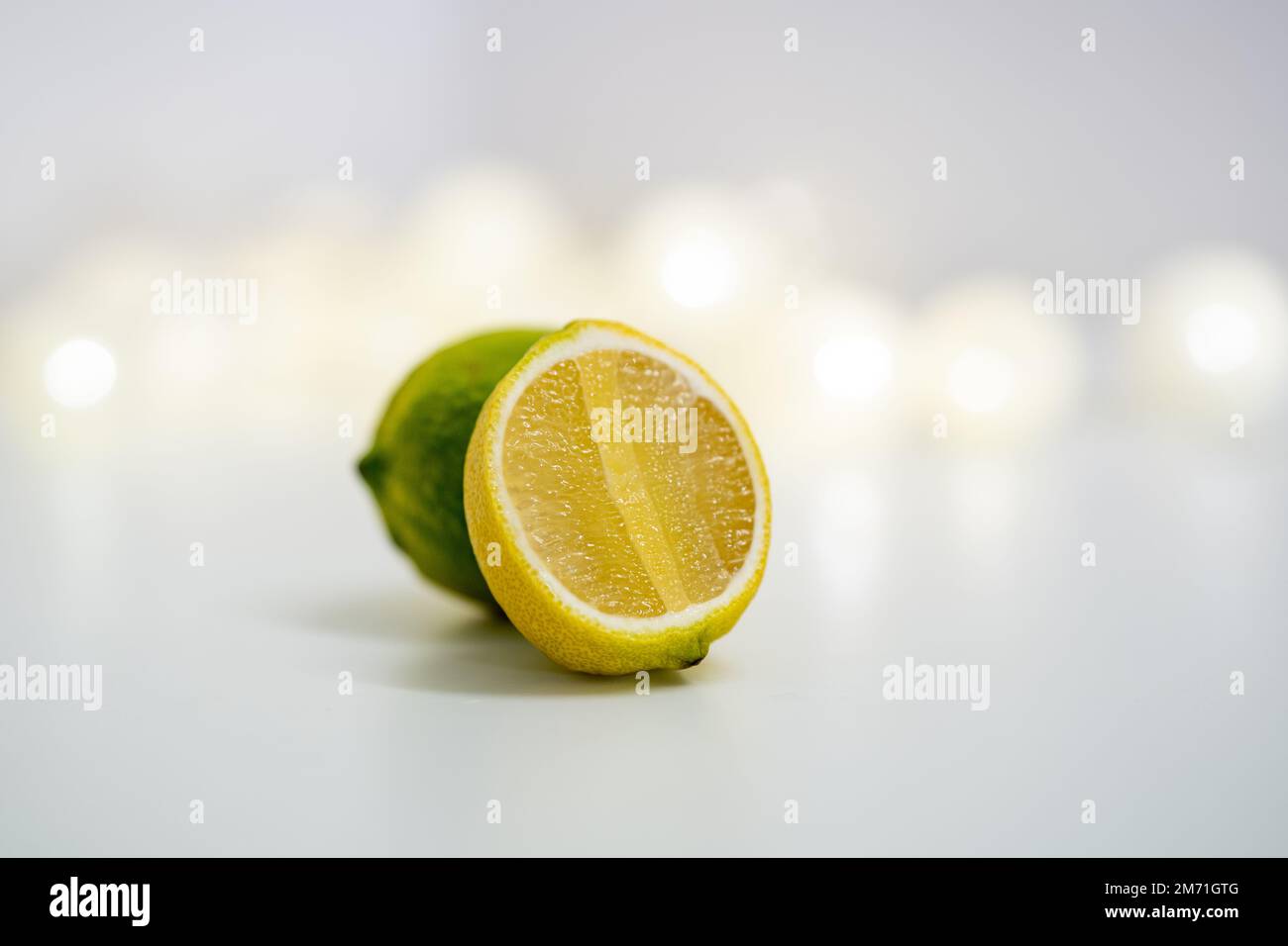 Half a lemon is placed on top of a whole lemon. White background with ...
