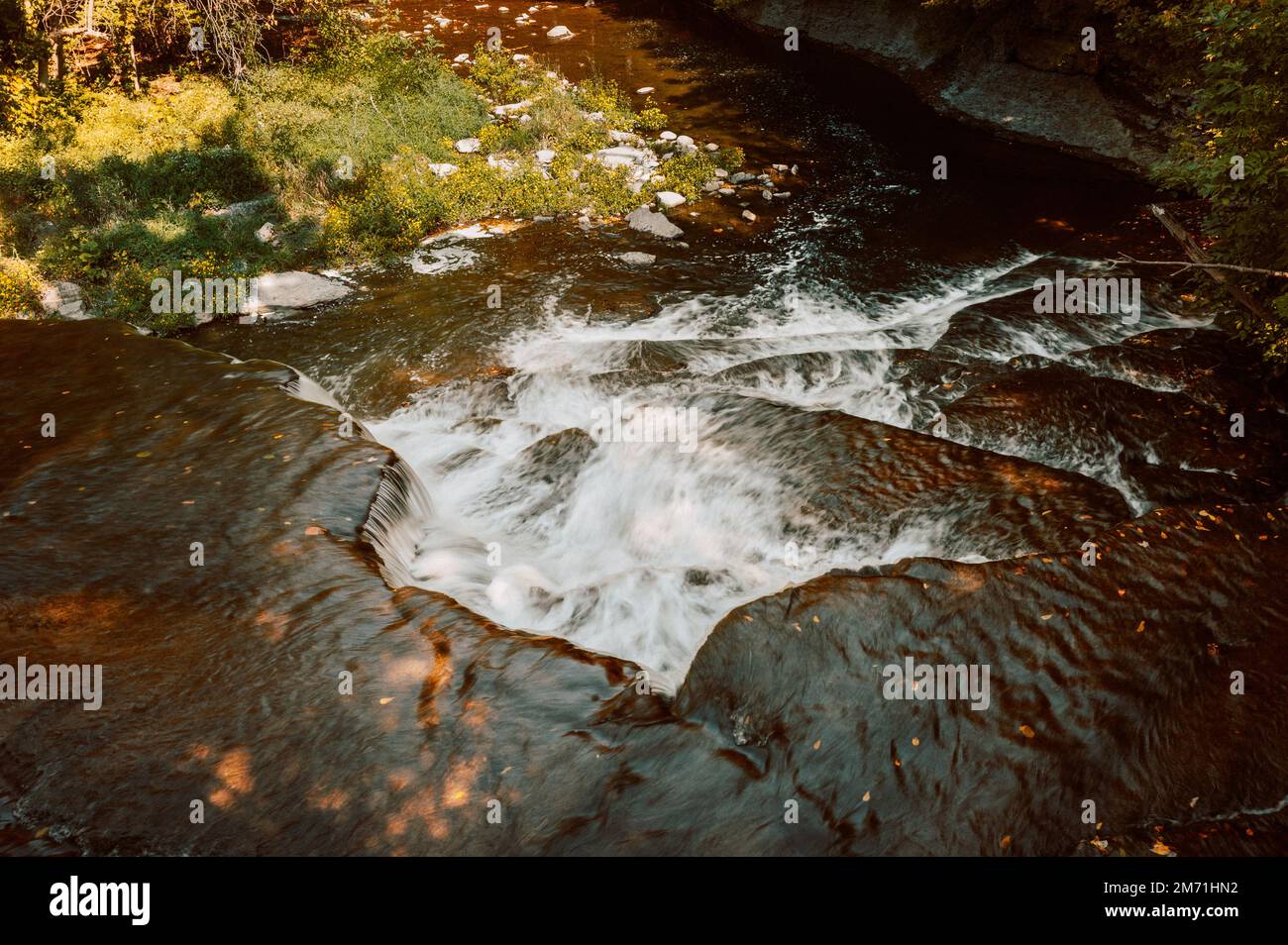 Fall leaves along the river, water flowing from a waterfall in Autumn ...