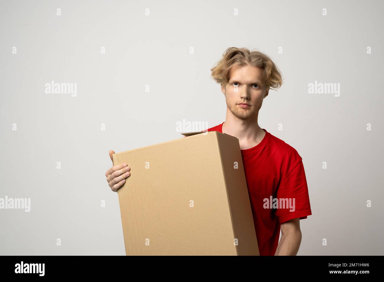 Young courier man in red uniform carrying a box, parcel. Delivery ...