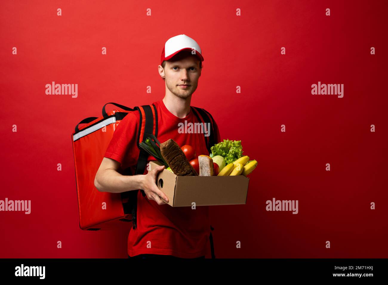 Proffesional young delivery man in red uniform carrying package box of ...