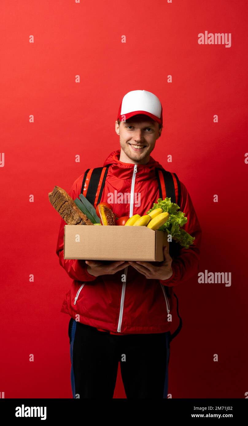 Fast young delivery man in red uniform carrying package box of grocery ...