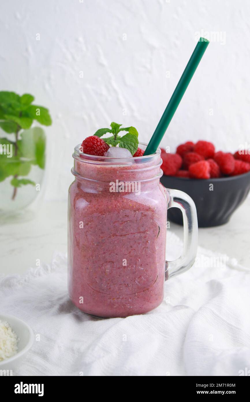raspberry coconut smoothie with ice in a jar with straw, white ...