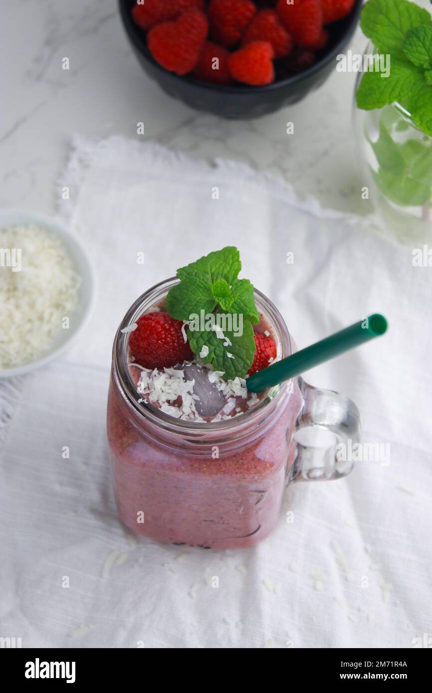 raspberry coconut smoothie with ice in a jar with straw, white ...