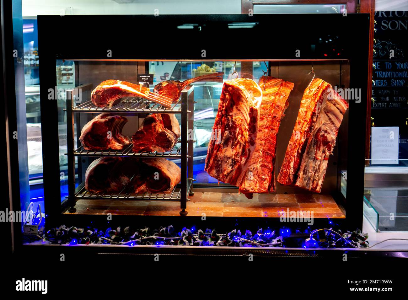Cuts of meat in a butchers shop window with Christmas holly lit up at ...