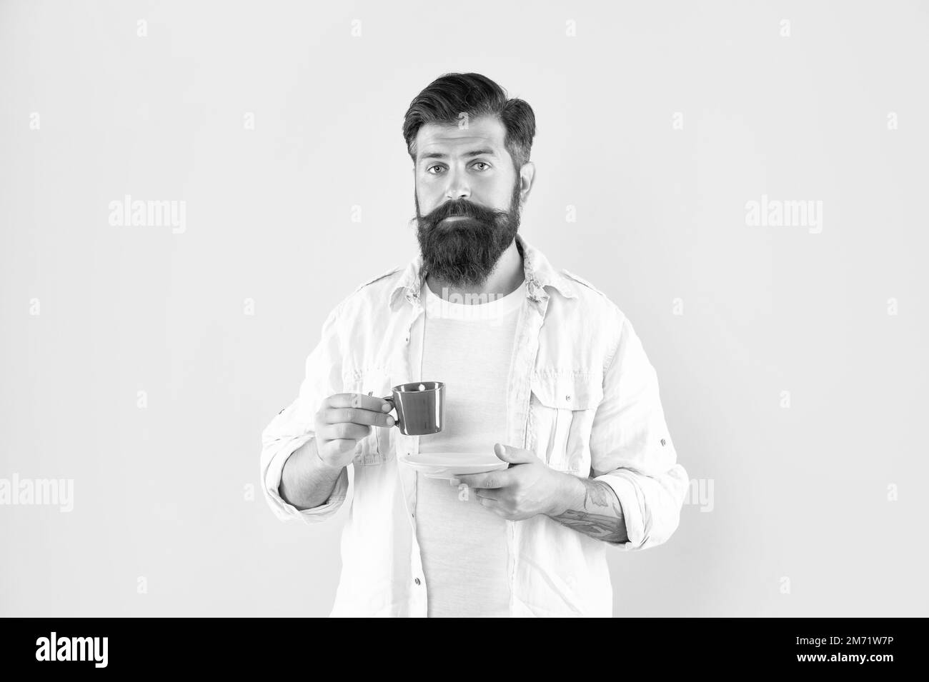 Serious guy drinking coffee from cup holding saucer yellow background ...