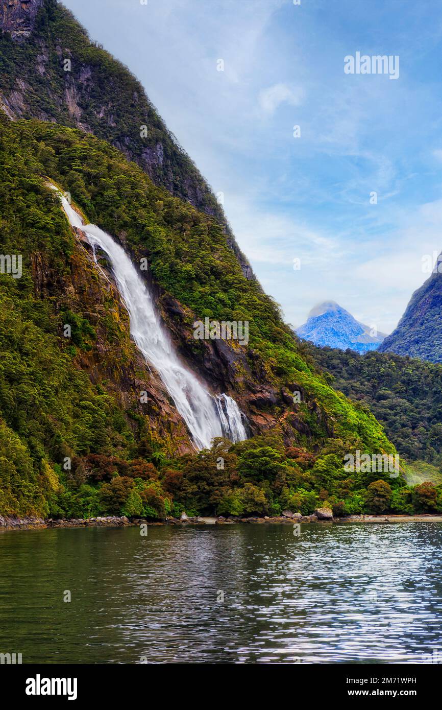 Bowen waterfall flowing down to fiord waters of Milford Sound in New ...