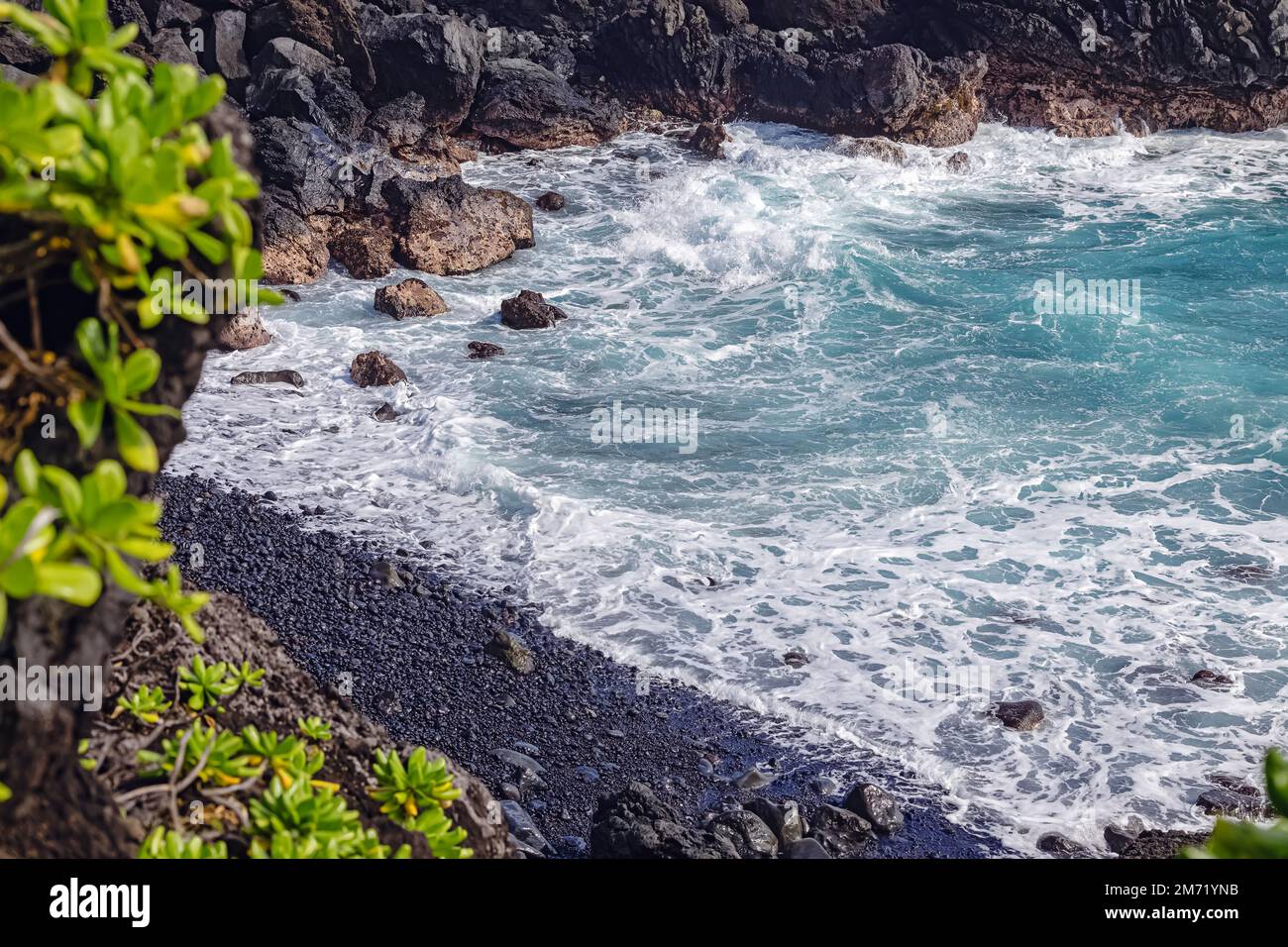 Small isolated beach with black stones and blue waves on Maui island ...