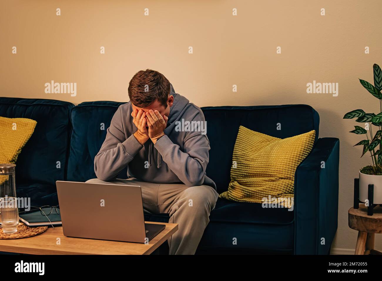 Frustrated man sitting on the sofa in front of his laptop. Covering ...