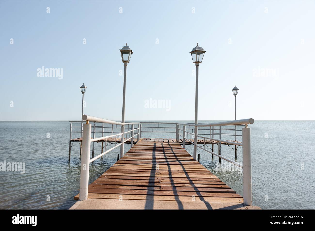 Wooden and metal pier with lampposts during a cloudless summer day with ...
