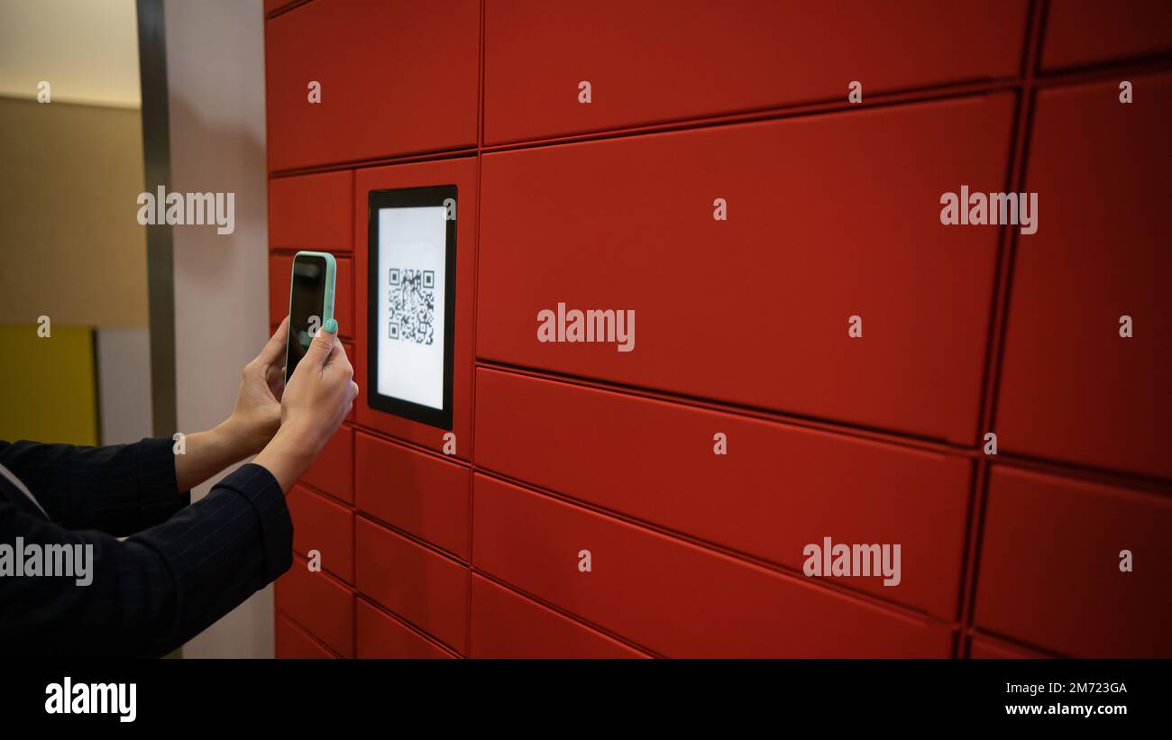 A woman scans a red code to pick up a parcel at a parcel machine ...