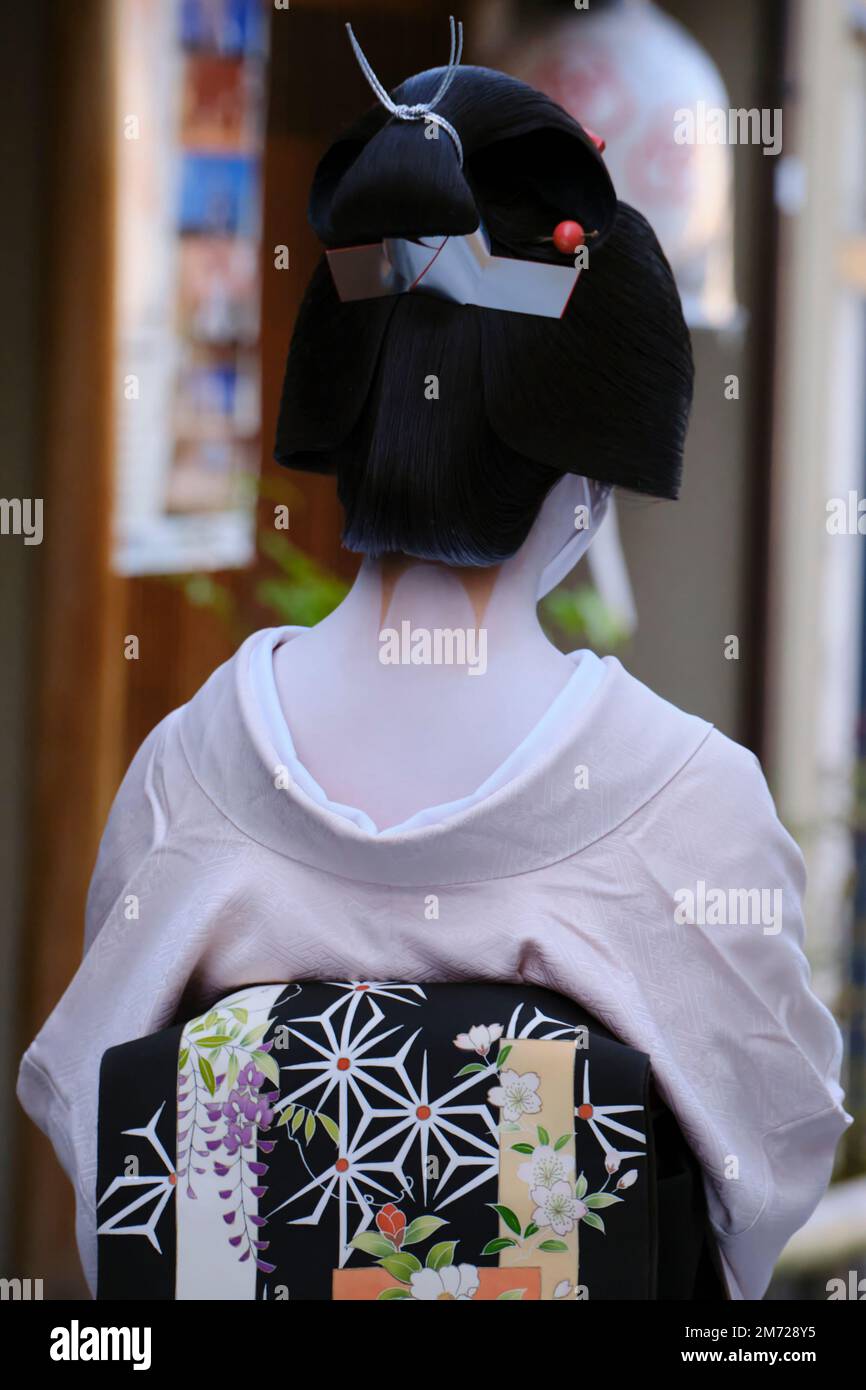 A geisha wearing a mask and light pink kimono walks down the street in ...