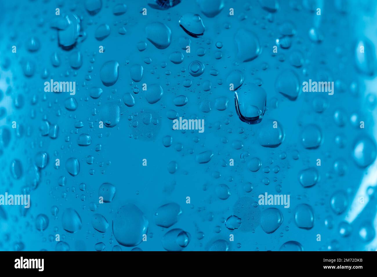 Water pouring from a plastic bottle into a glass beaker on a blue ...