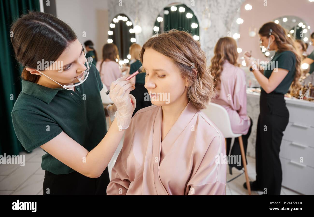 Female beauty specialist applying eyeshadow on client eyelid with ...