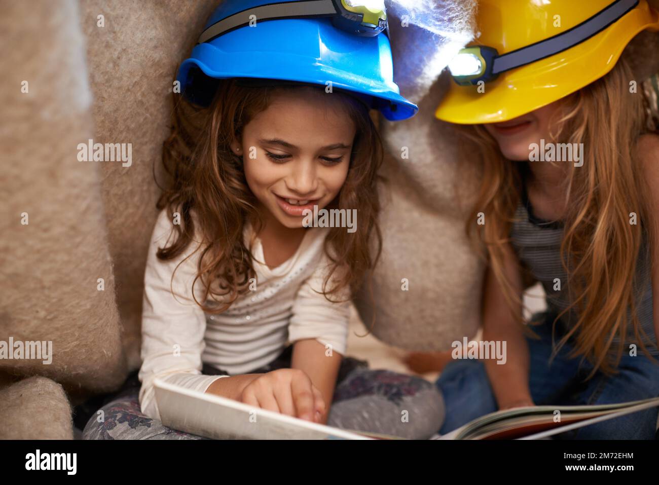 Sleepover stories. two little girls reading underneath a blanket using ...